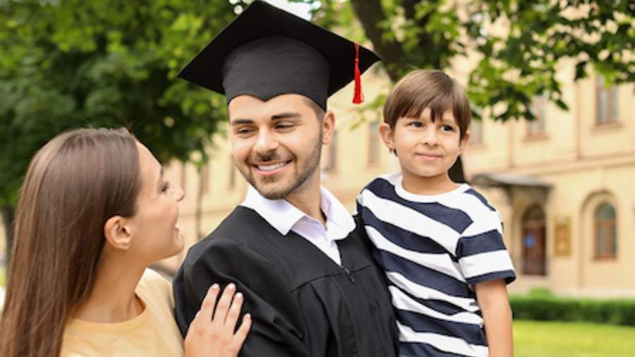 White male in a cap and gown at his graduation ceremony with his wife ...