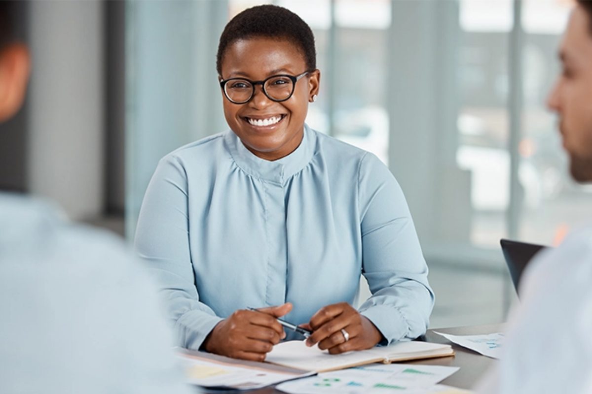 Black woman smiling at two coworkers sitting across from her with their ...